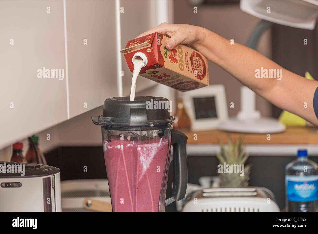 Close up view of female's hand pouring milk into blender with smoothie ...