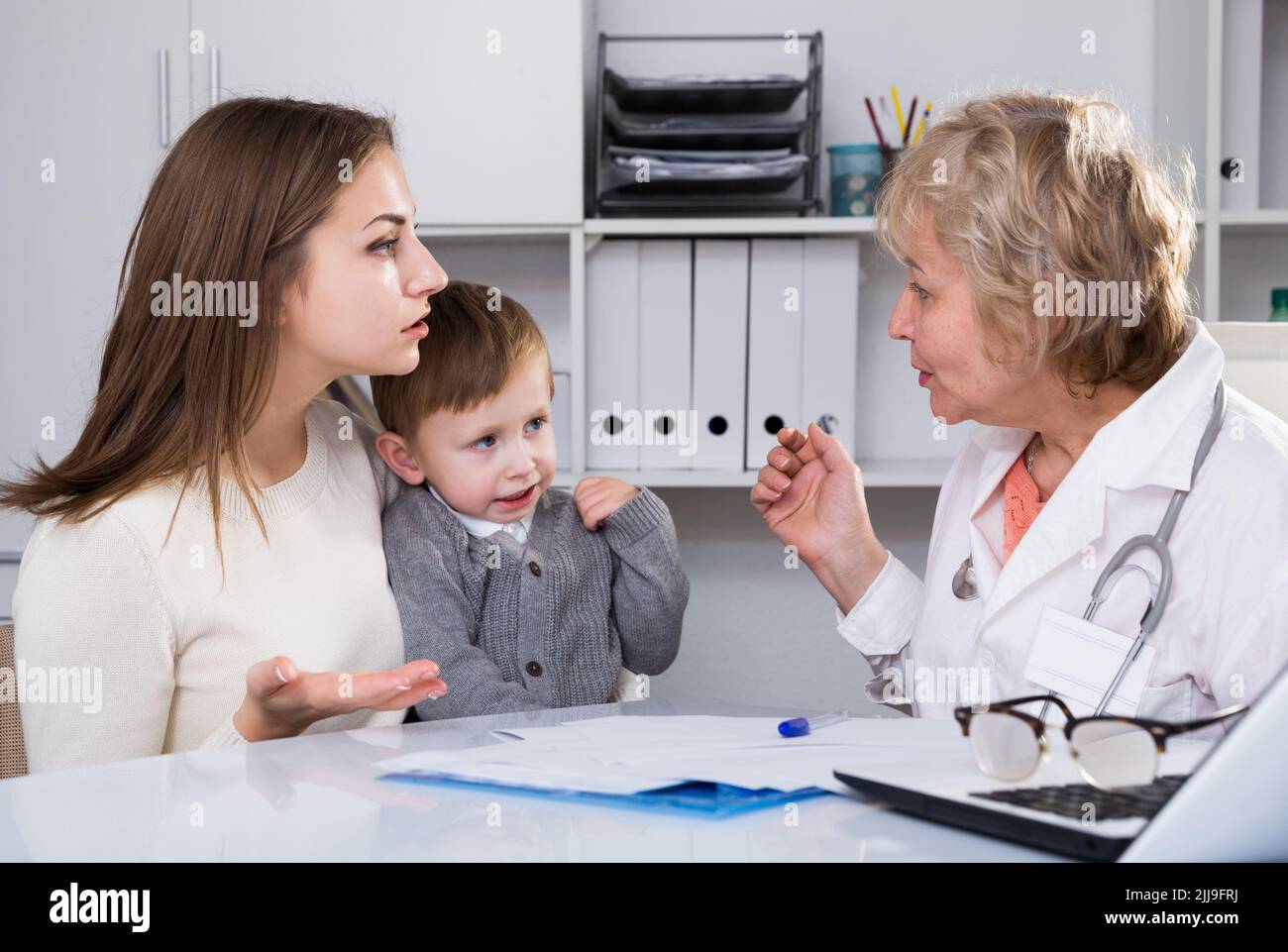 Pediatrist woman is examining kid and talking to his puzzled mother ...