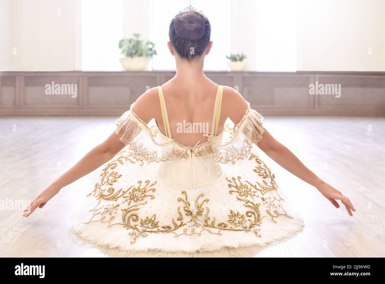 Back view of beautiful young ballet dancer in cream dress sitting and ...