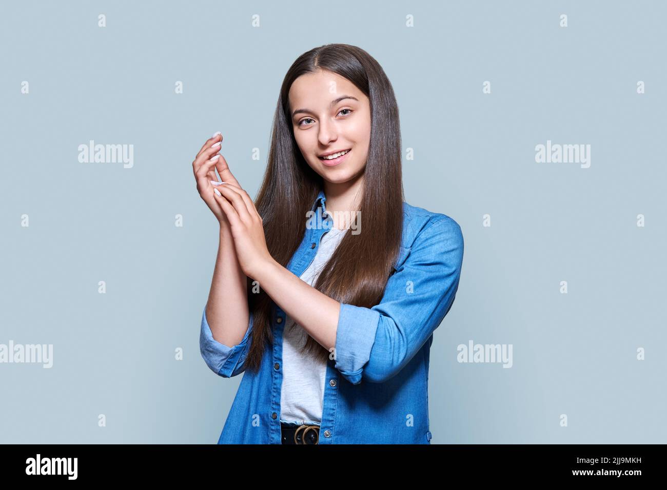 Attractive teenage girl clapping hands on light gray color studio ...
