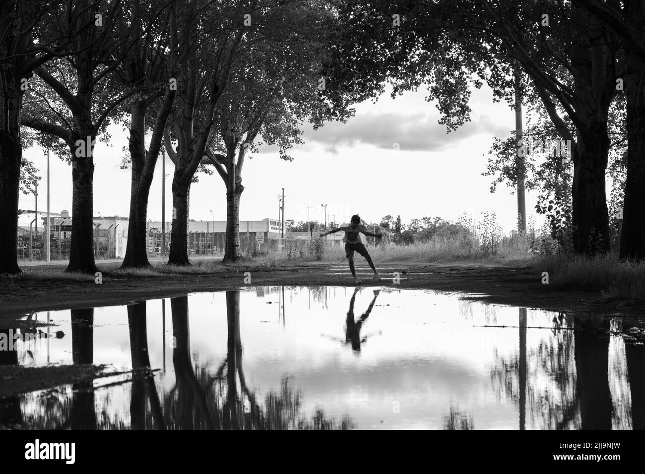 A Caucasian kid jumping over a pond in a park in grayscale Stock Photo ...
