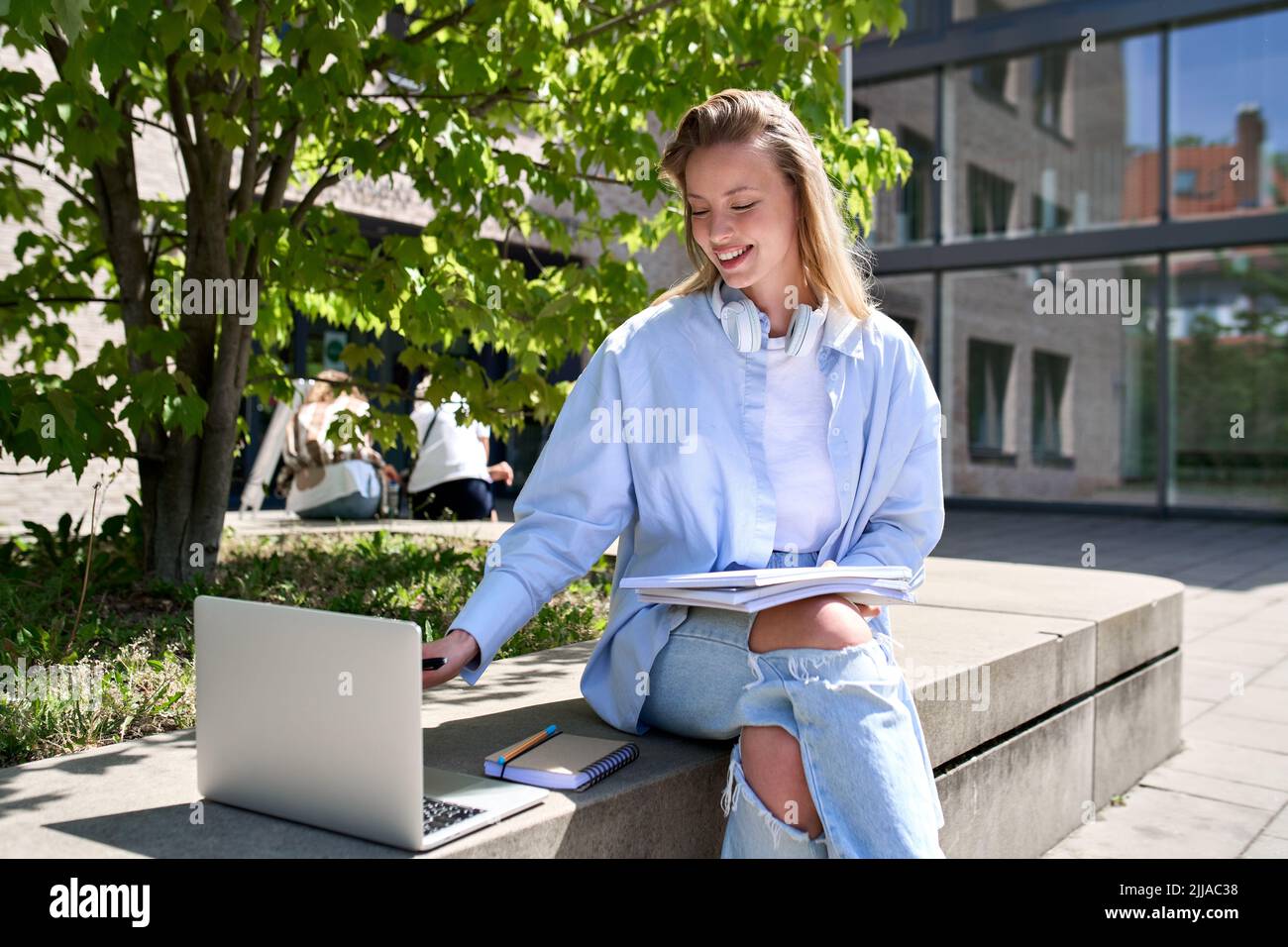Smiling girl student using laptop studying outdoor in university campus ...