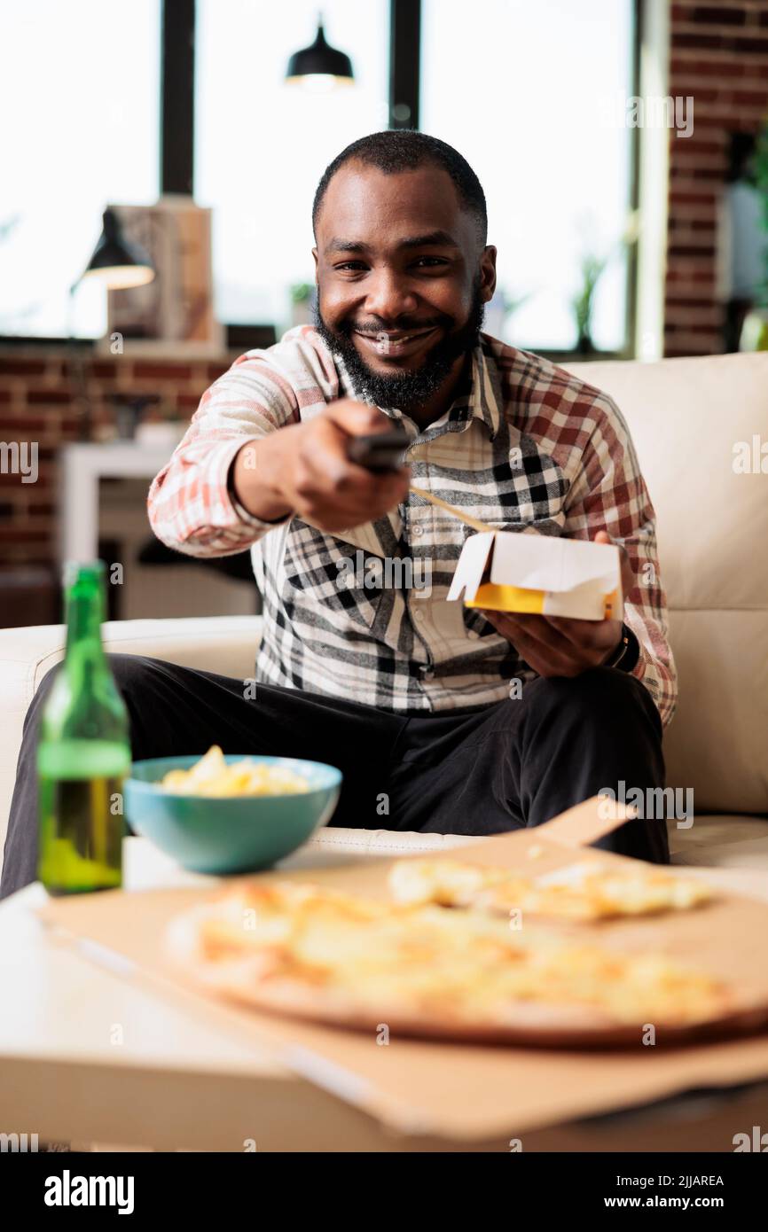 Young man holding noodles delivery box and switching tv channels with ...