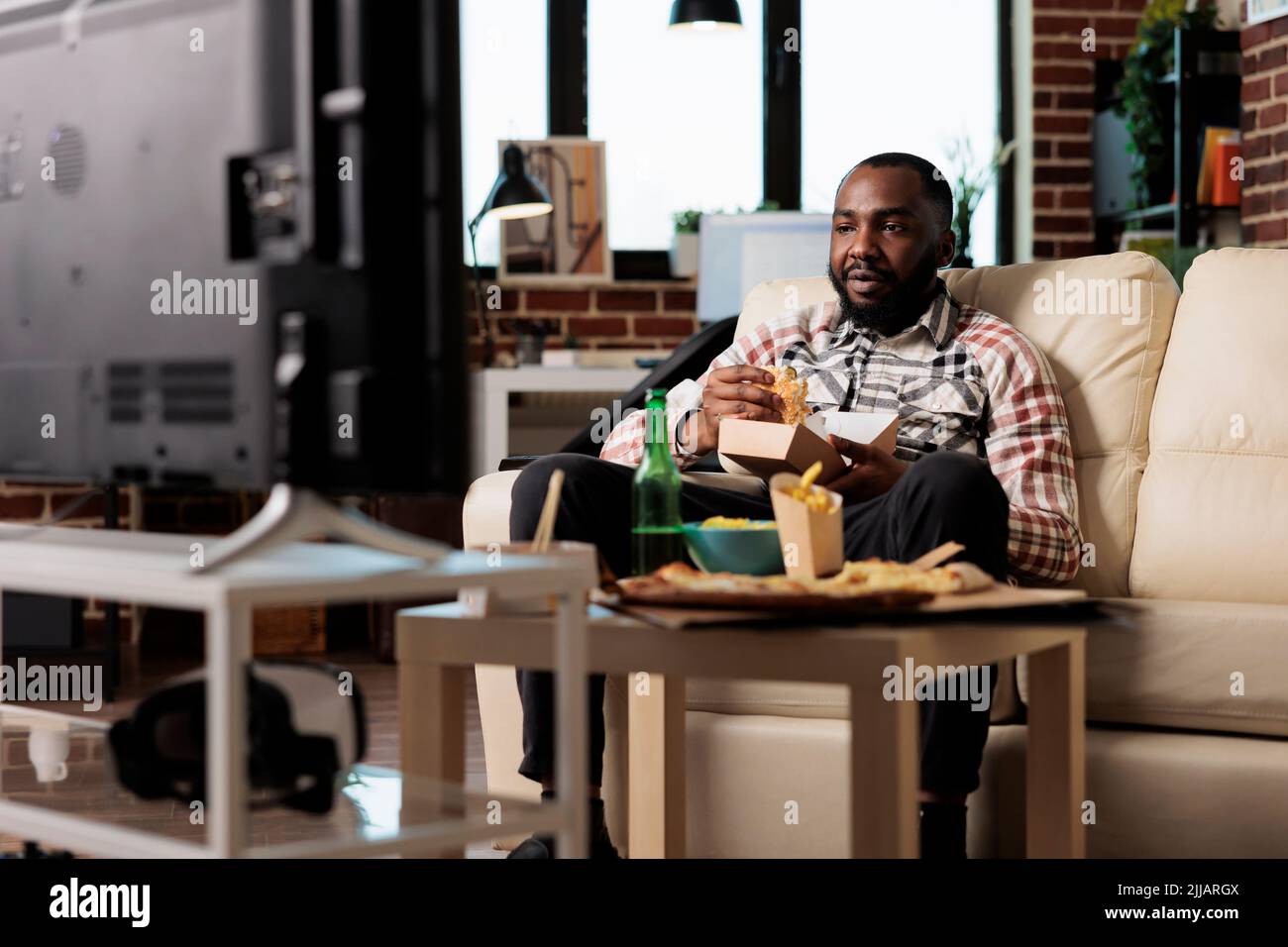 Young adult eating fast food delivery meal at home, watching film on ...