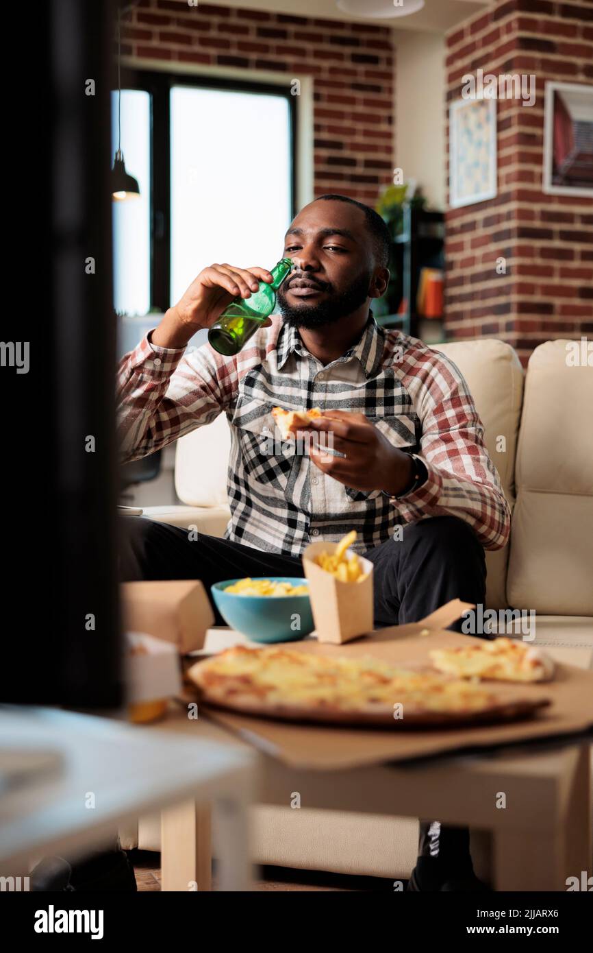 Cheerful man drinking alcoholic beer from bottle and eating takeaway ...