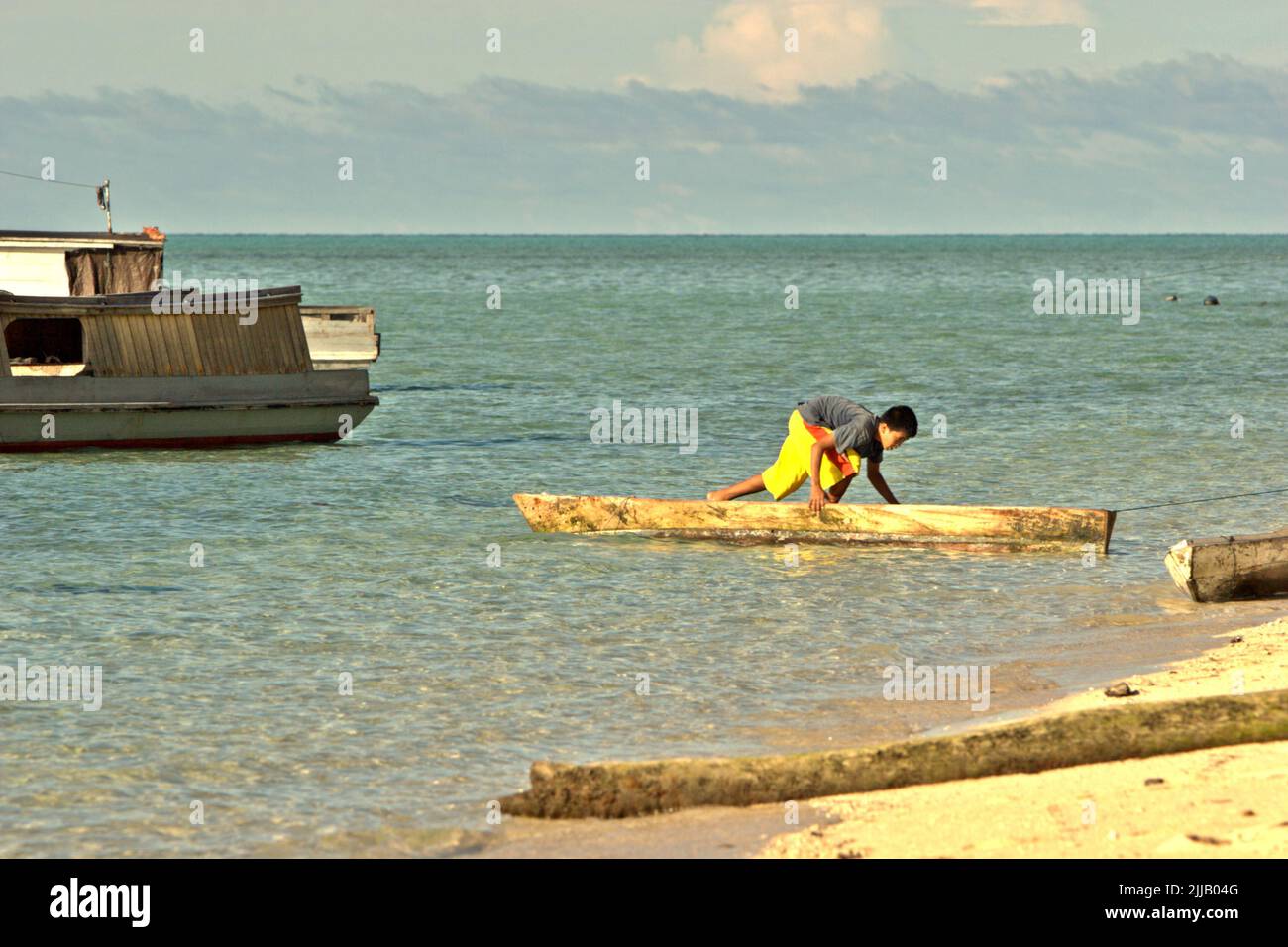 A child stepping on a log on the coastal water of Derawan Island, a ...