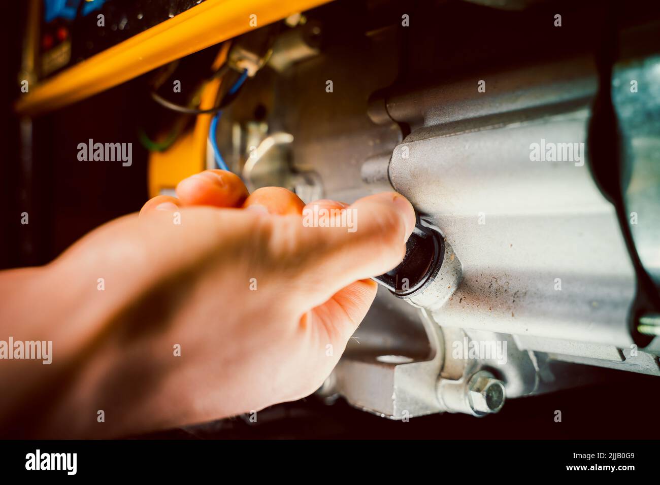 A hand unscrews the oil filler cap of an electric gas generator close ...