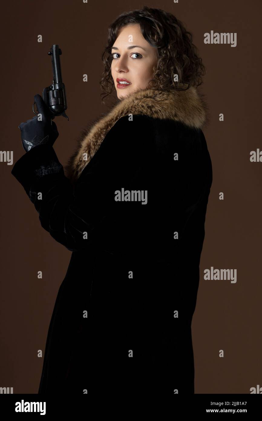 A 1920s woman wearing a velvet coat with a fur collar and holding a gun ...