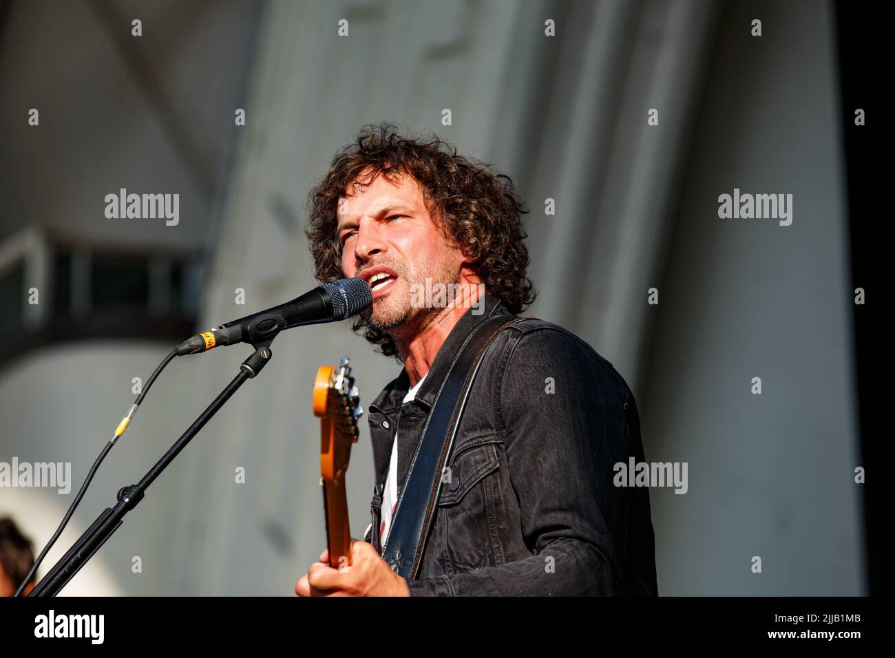 Sam Roberts plays guitar and sings on stage wearing a denim jacket and ...