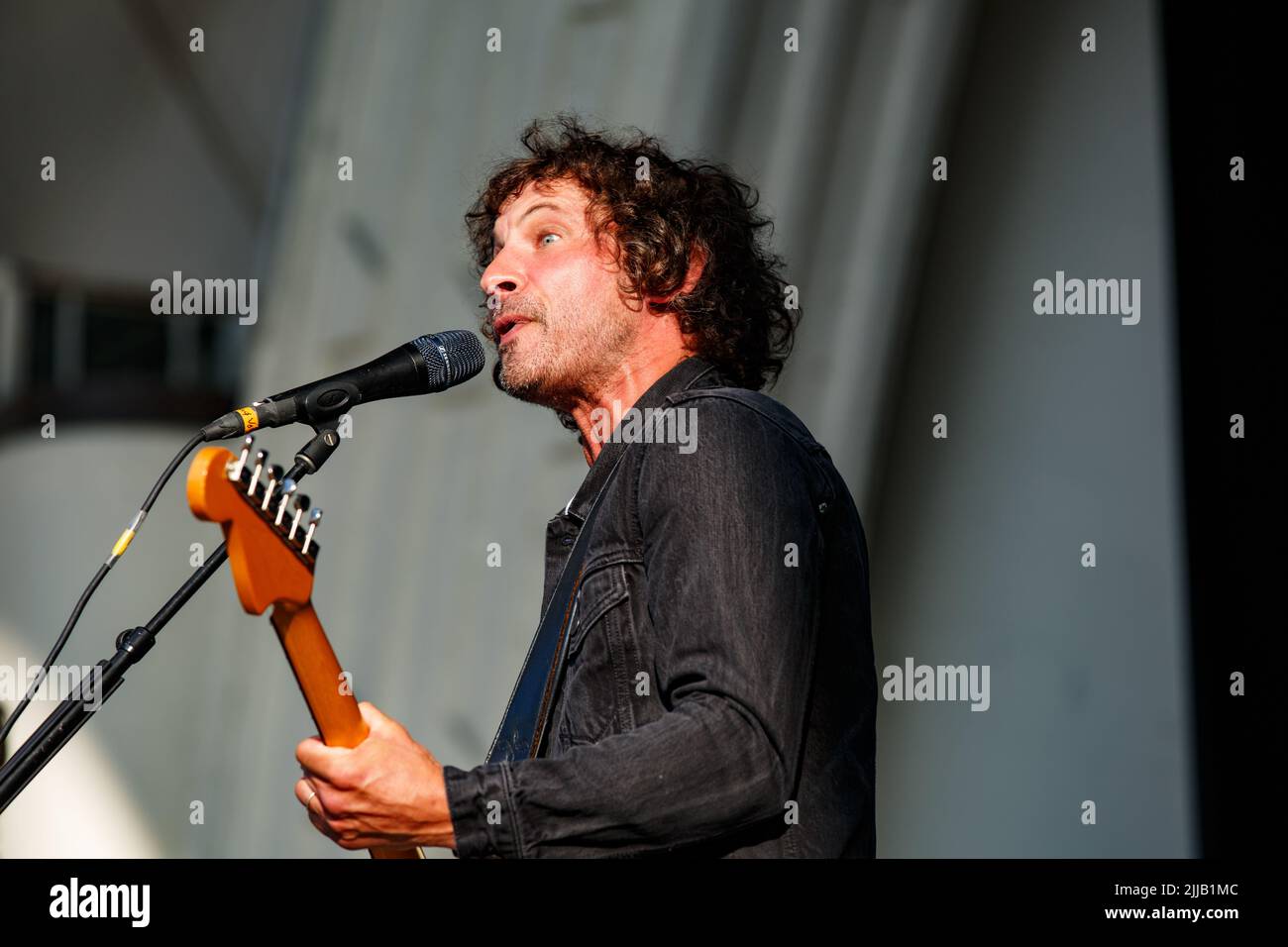Sam Roberts plays guitar and sings on stage wearing a denim jacket and ...