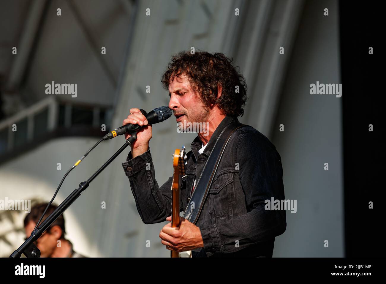 Sam Roberts plays guitar and sings on stage wearing a denim jacket and ...