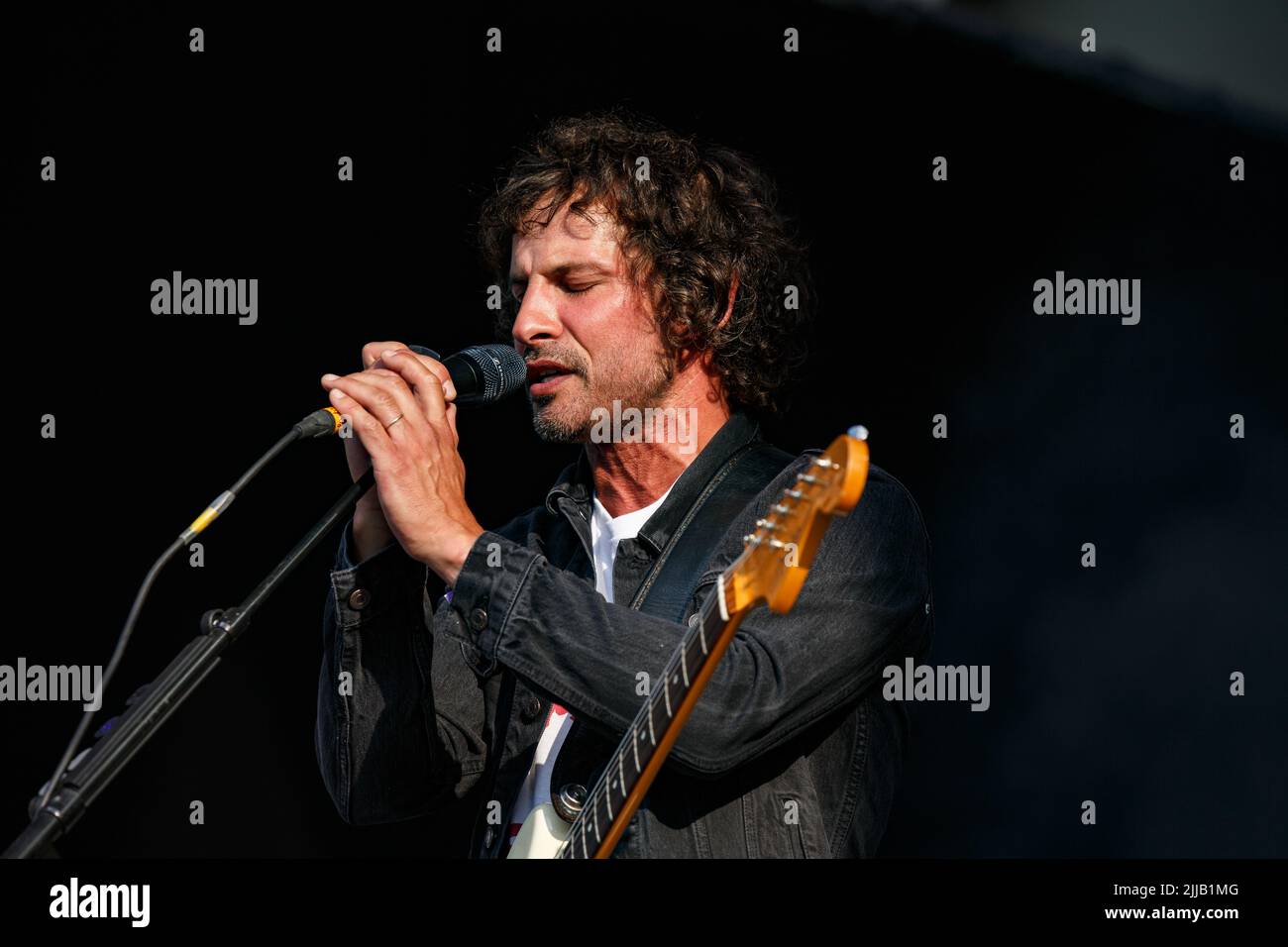 Sam Roberts plays guitar and sings on stage wearing a denim jacket and ...