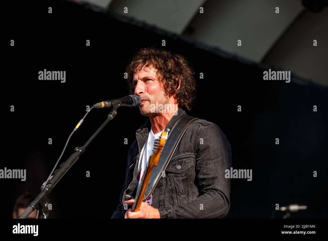 Sam Roberts plays guitar and sings on stage wearing a denim jacket and ...