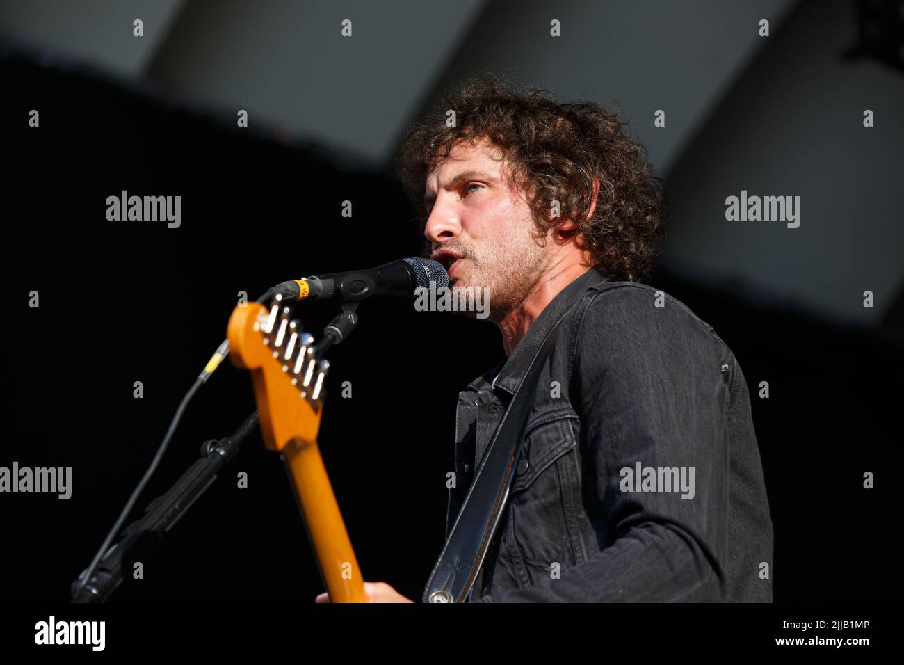 Sam Roberts plays guitar and sings on stage wearing a denim jacket and ...