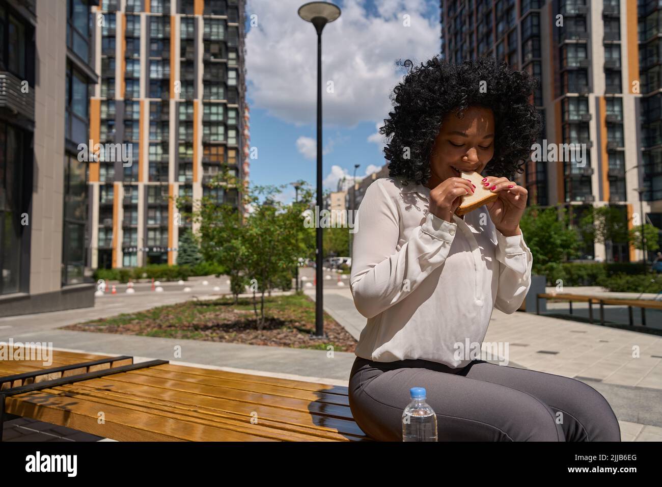 Multiracial female eating a sandwich while sitting on a bench Stock ...