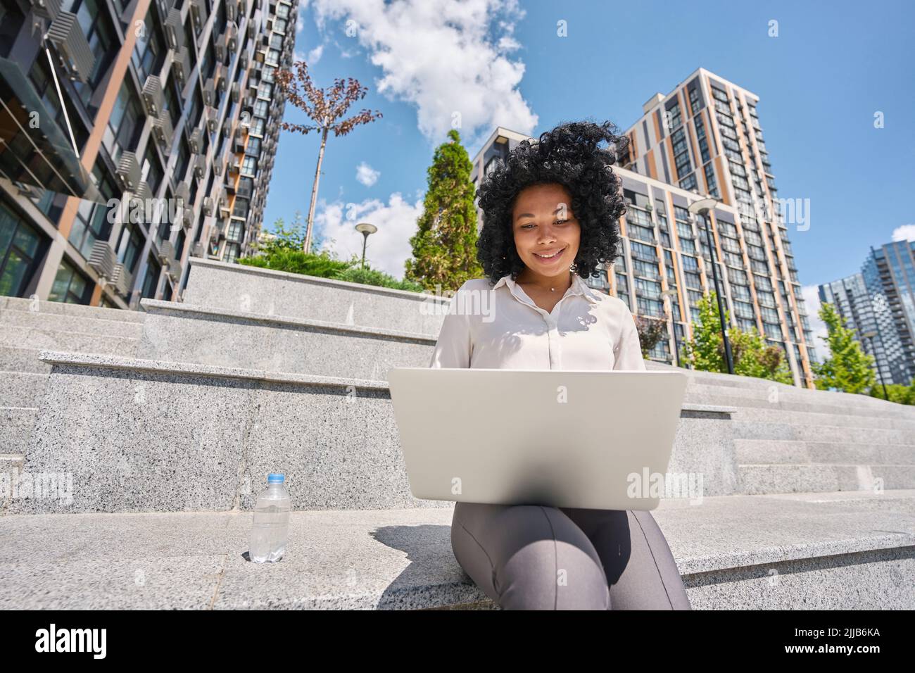 Smiling mixed race female sits with laptop on granite steps Stock Photo ...