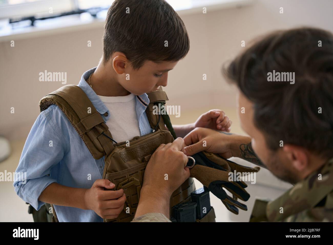 Army man fastening gloves to tactical vest on his son Stock Photo - Alamy