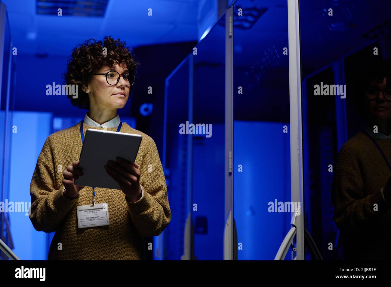 Young female engineer using tablet while walking in corridor of data center and checking ...