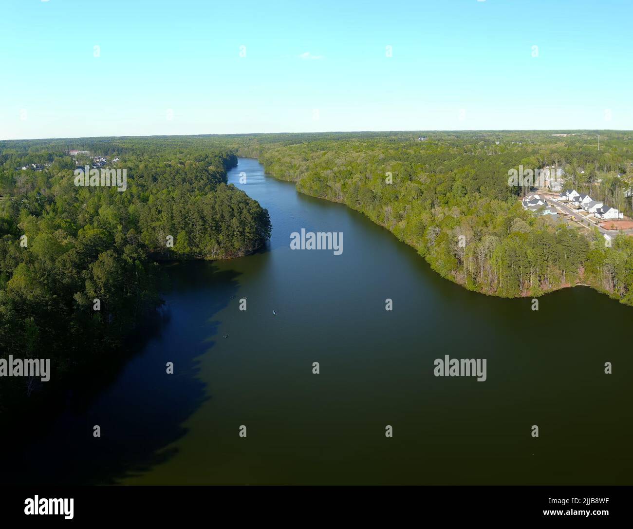 A drone view of a wide river surrounded by dense forests under the blue ...