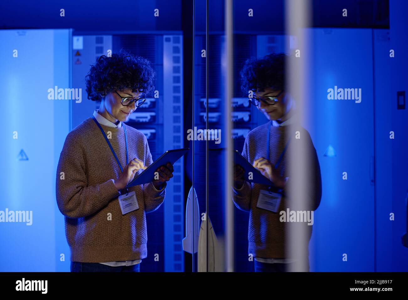 Female IT administrator walking in server corridor diagnosing hardware ...