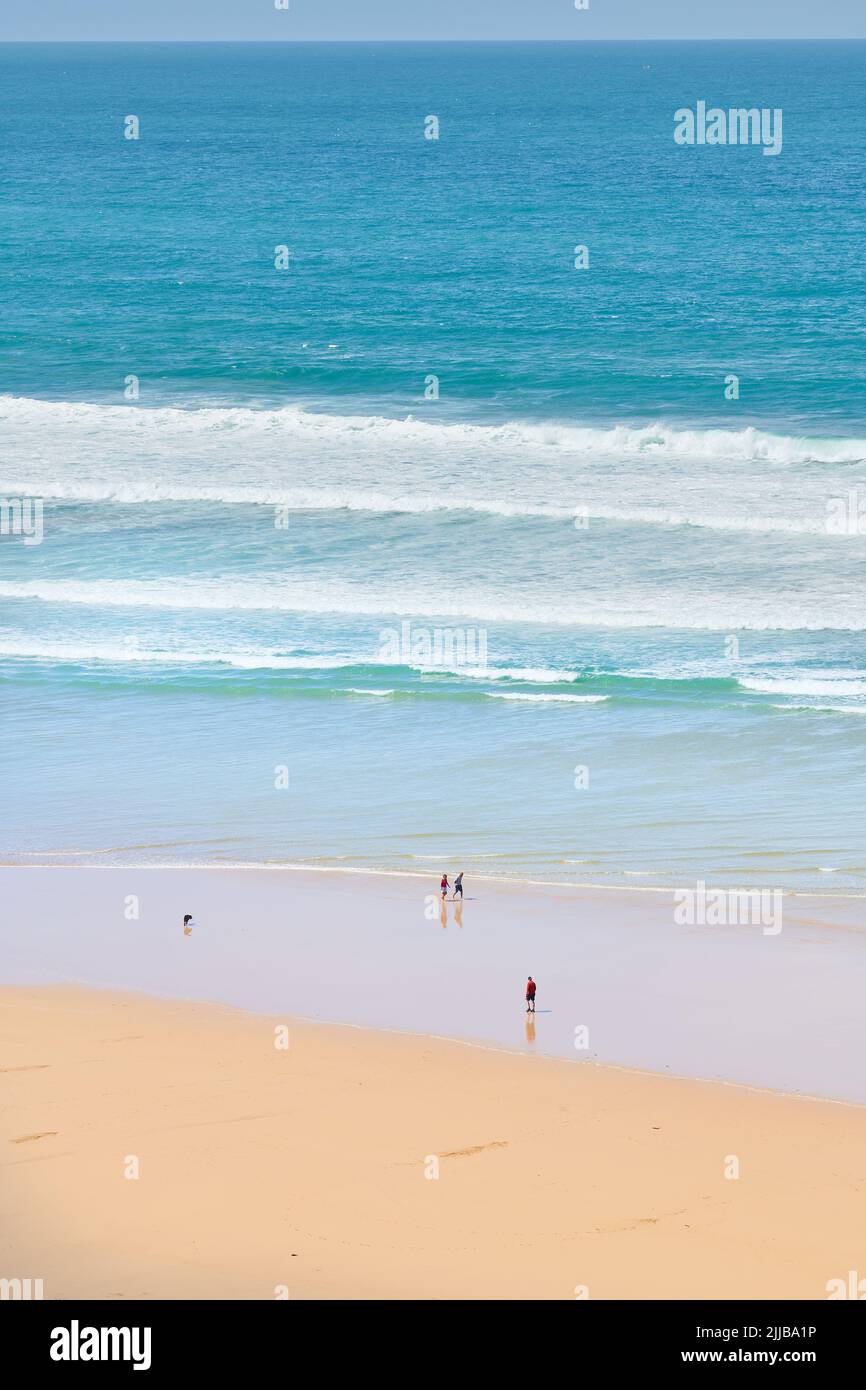 Holiday makers on the shore where surf waves from the Atlantic ocean ...