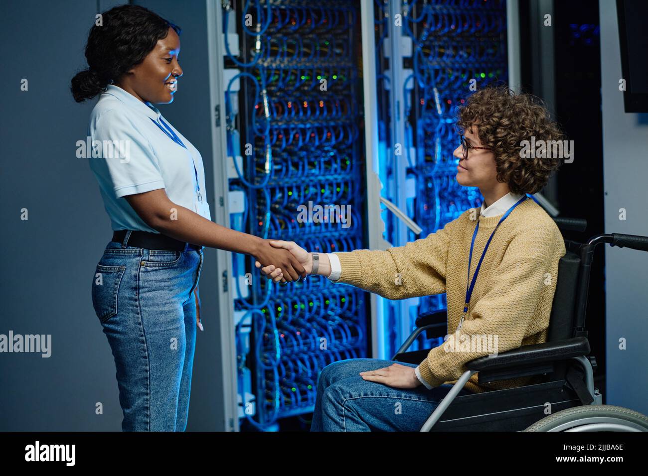 African IT engineer shaking hands with server worker in wheelchair during their work in data ...
