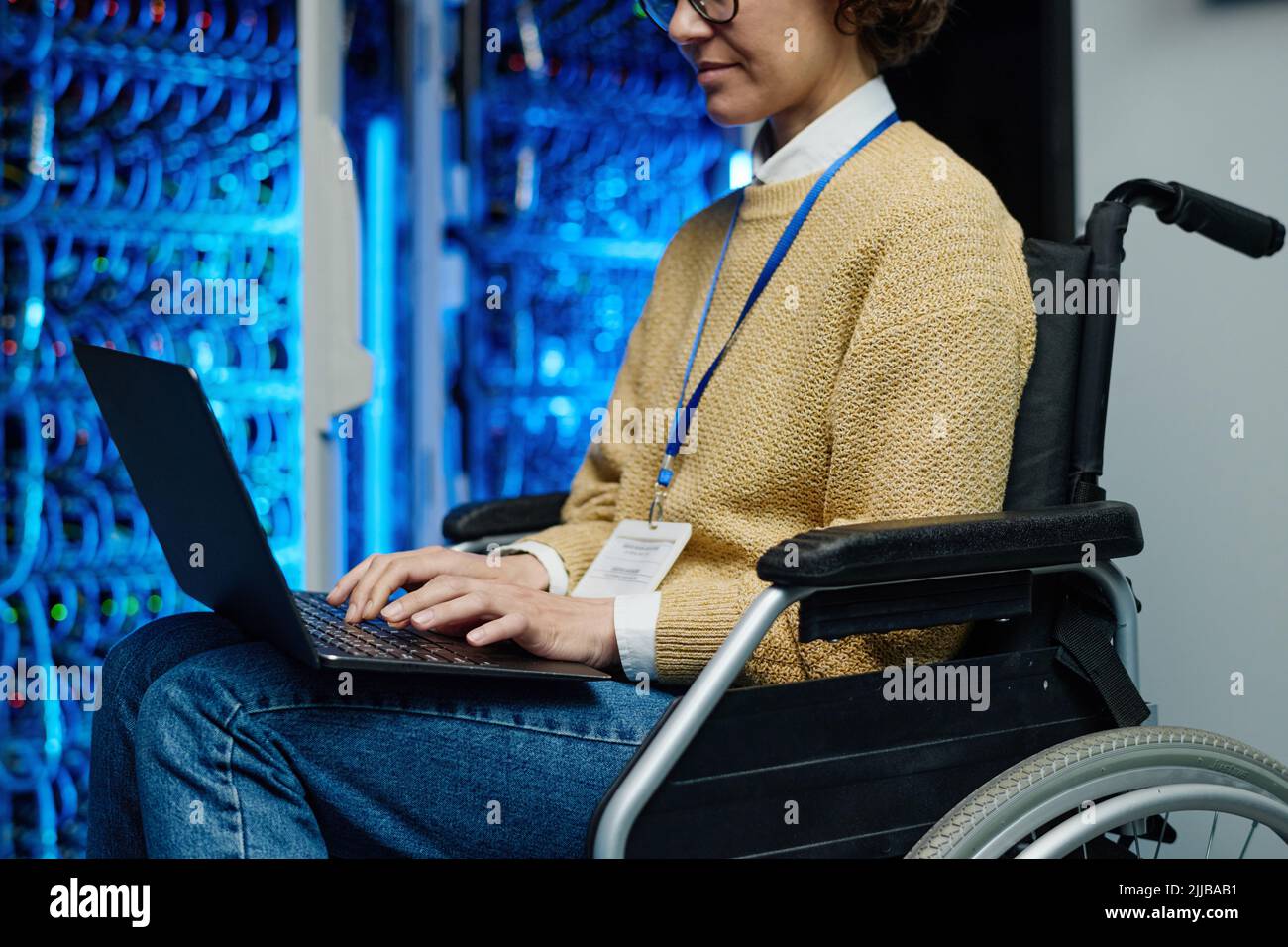 Close-up of female engineer with disability sitting in wheelchair and typing on laptop, she ...