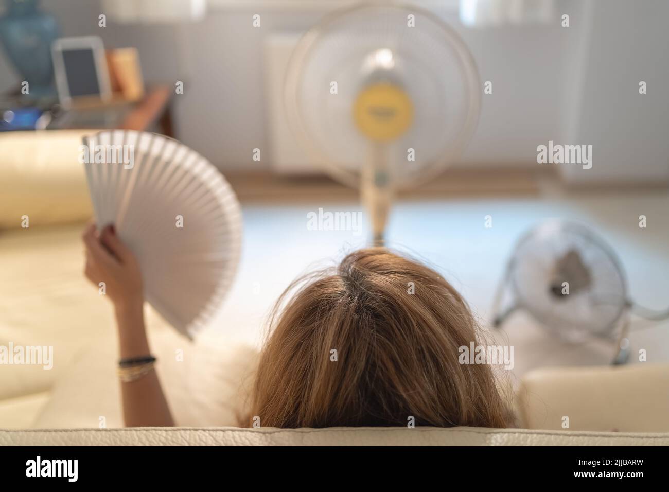 Woman sitting on a sofa with several fans giving her air and a fan in ...