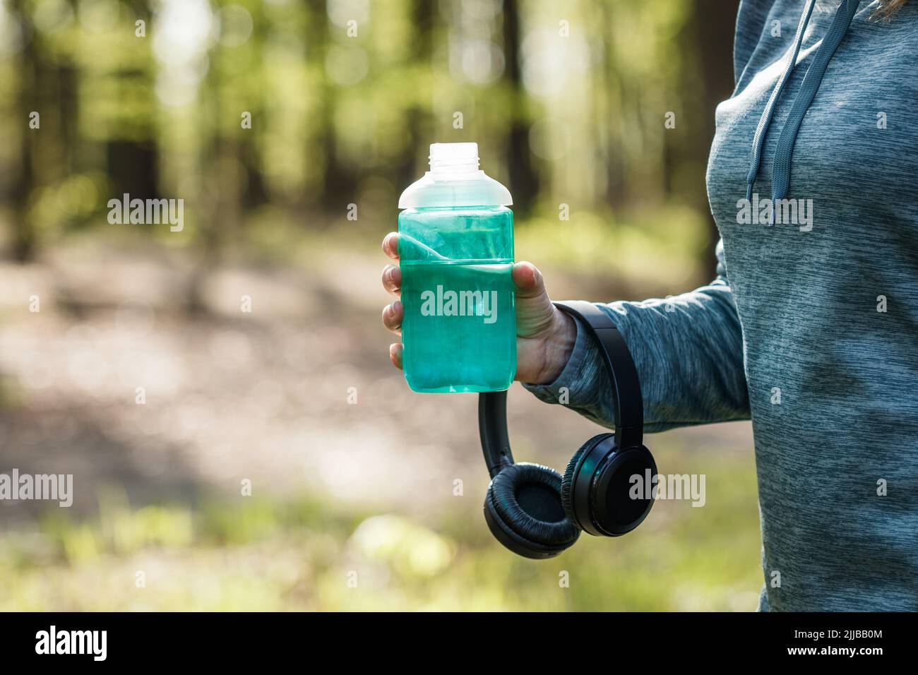 Woman drinking water from bottle and holding headphones. Resting during ...