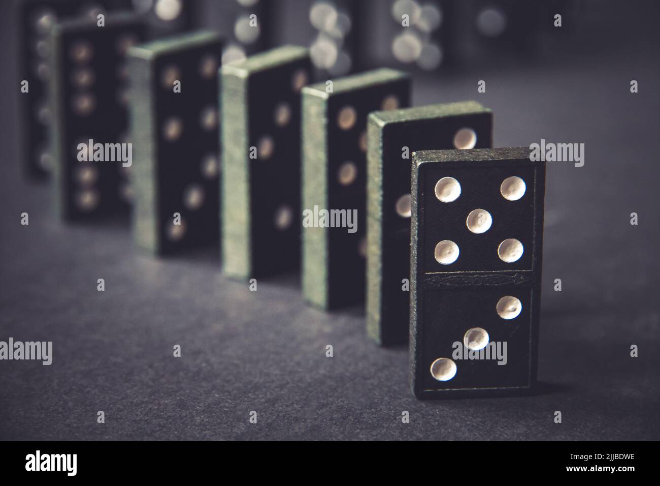 Black dominoes chain on a dark table background. Domino effect concept ...