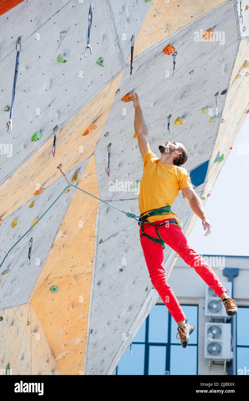 Sportsman climber hangs on one hand on an artificial climbing wall ...