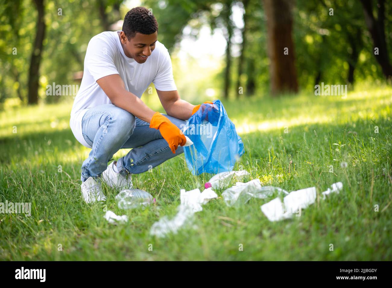Man crouching putting garbage in bag Stock Photo - Alamy