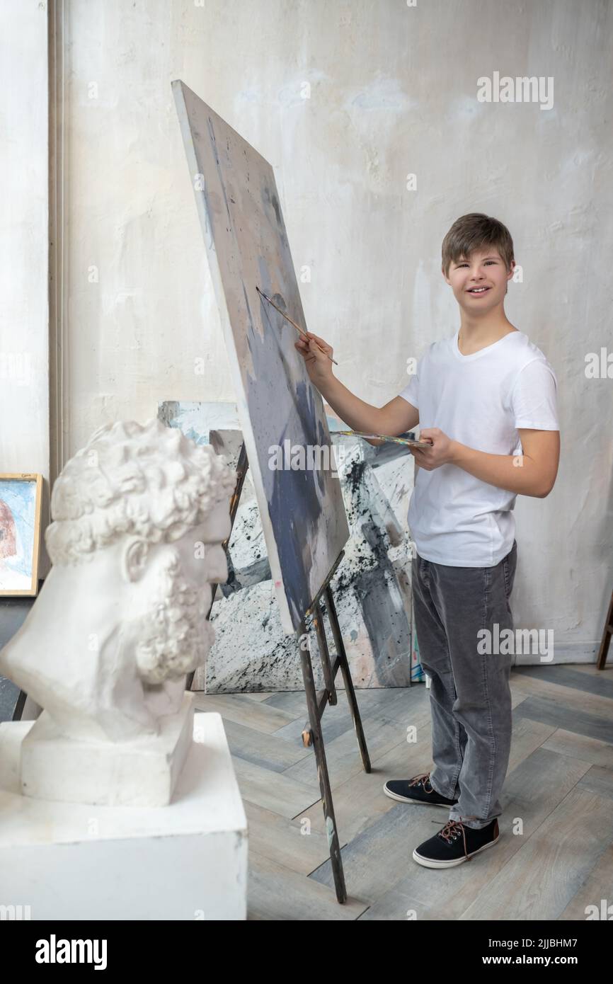 A boy with down syndrome painting in the studio and looking involved ...