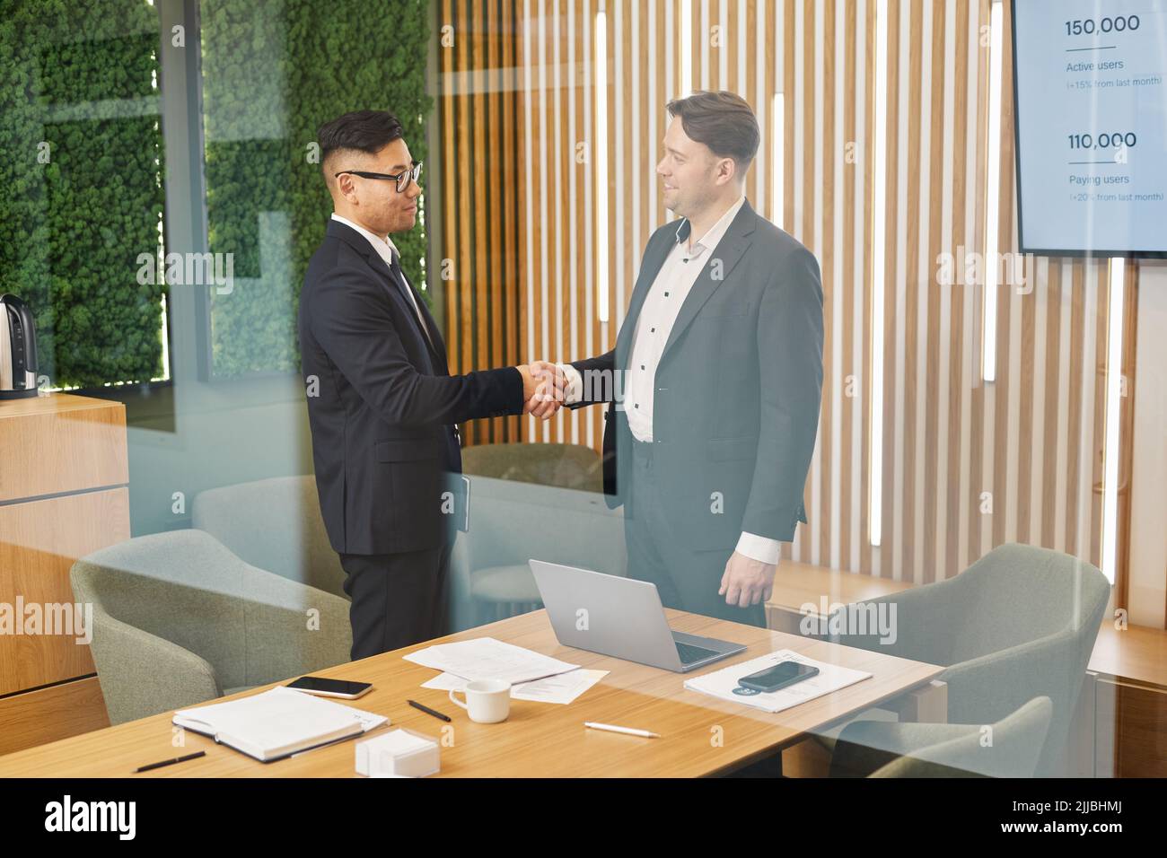 Side view portrait of two business partners shaking hands behind glass ...