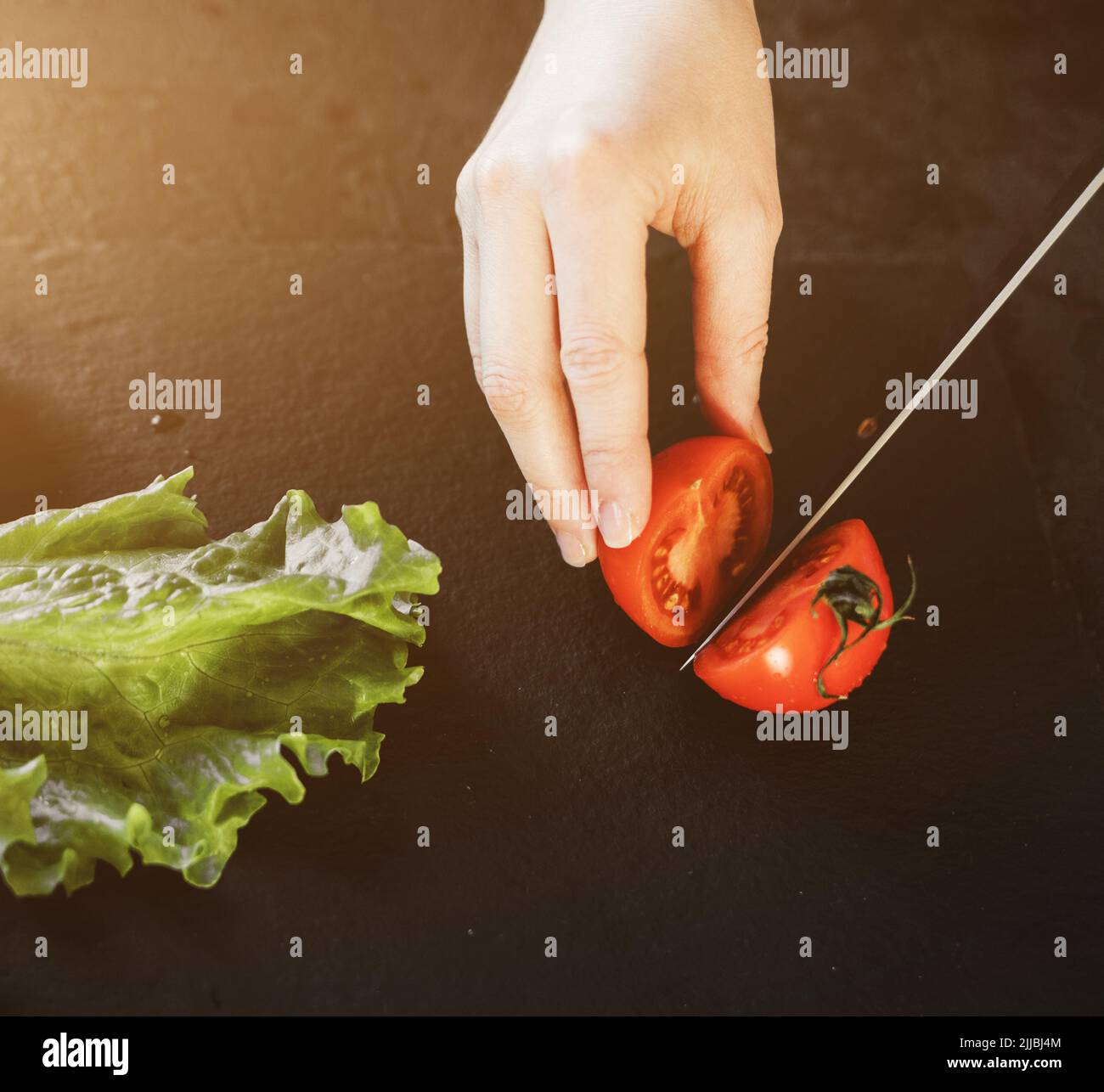 female hands, precisely slicing a fresh, red tomato on a black cutting ...