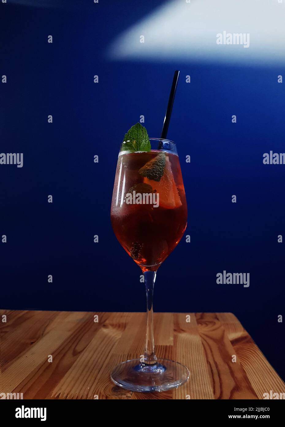 Aperol spritz in a glass with ice and orange on blue wall background ...