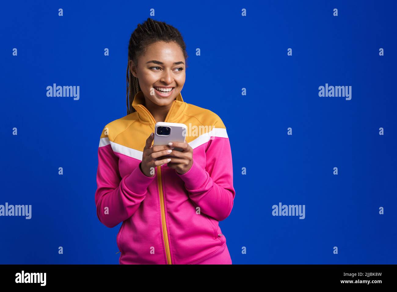 Black young woman laughing while using mobile phone isolated over blue ...