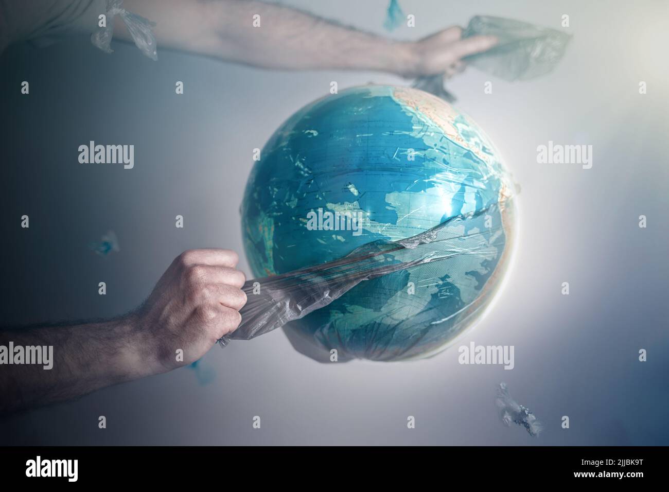 Men's hands tear off a plastic bag from the globe of planet Earth. The ...