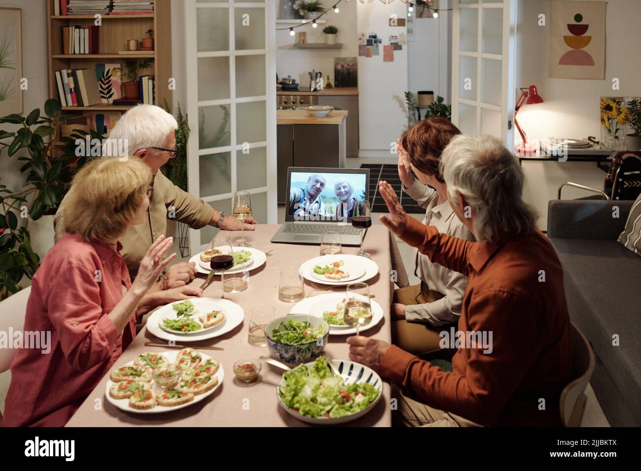 Group of senior friends waving hands while greeting aged couple on ...