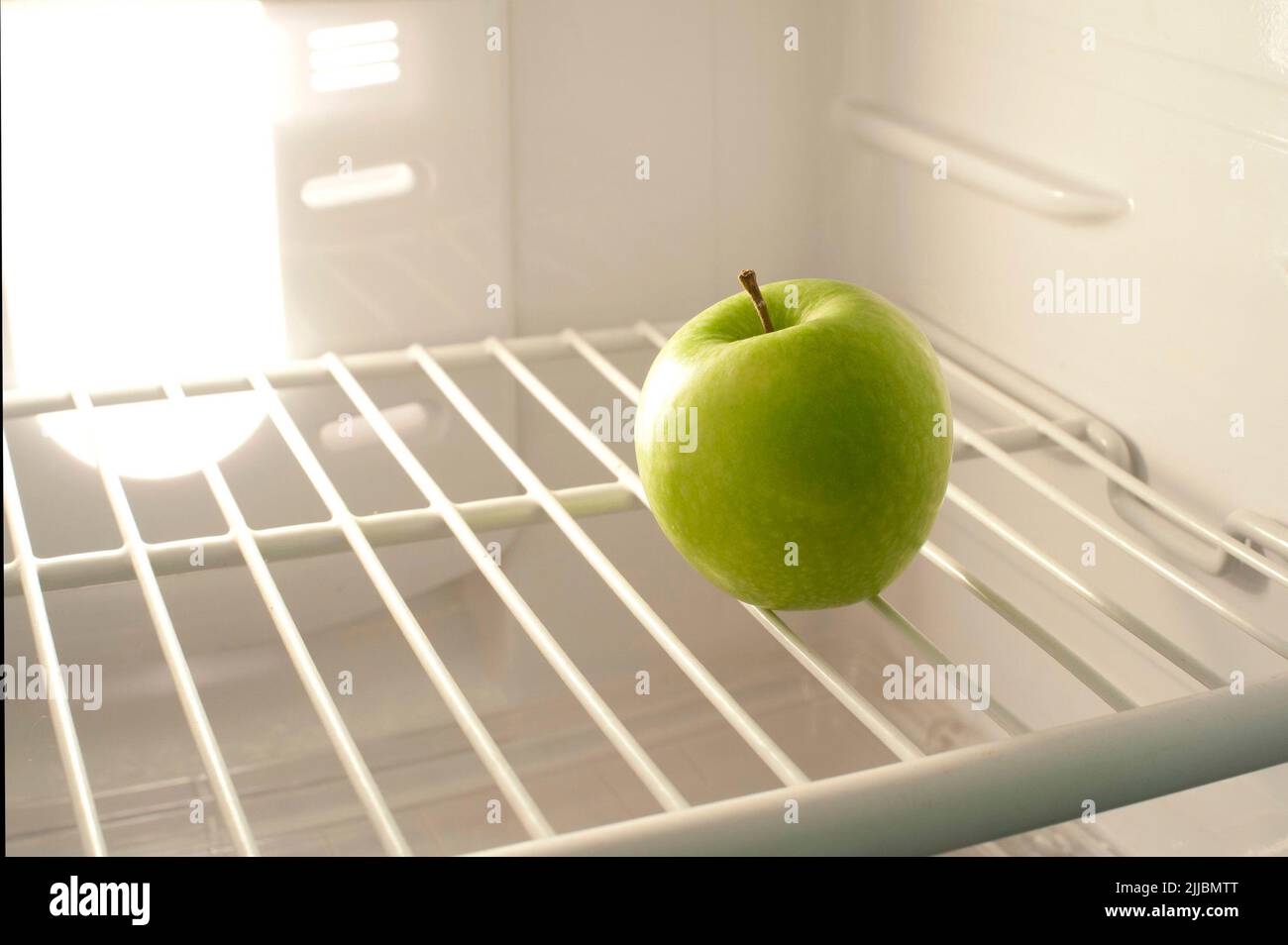 Interior of a small domestic refrigerator with a single green apple on ...