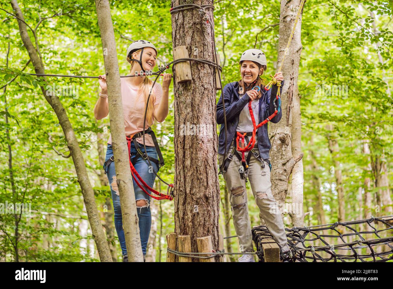 Two women girls female gliding climbing in extreme road trolley zipline ...