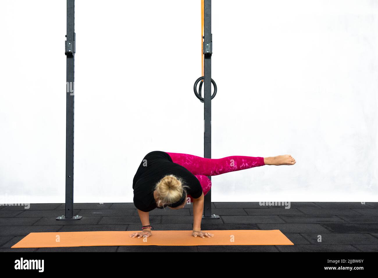 A blonde youth lady is performing the side one leg crow yoga posture ...