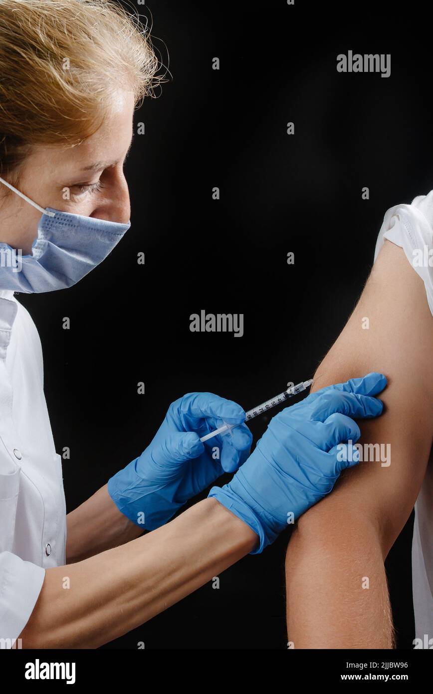 the doctor gives the shot in his hand on a black background. A female ...