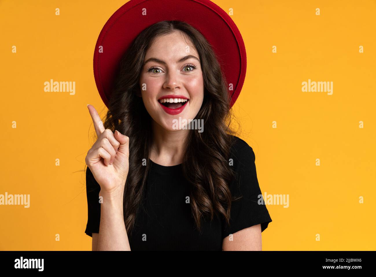 White young woman in red hat smiling while pointing finger upward ...