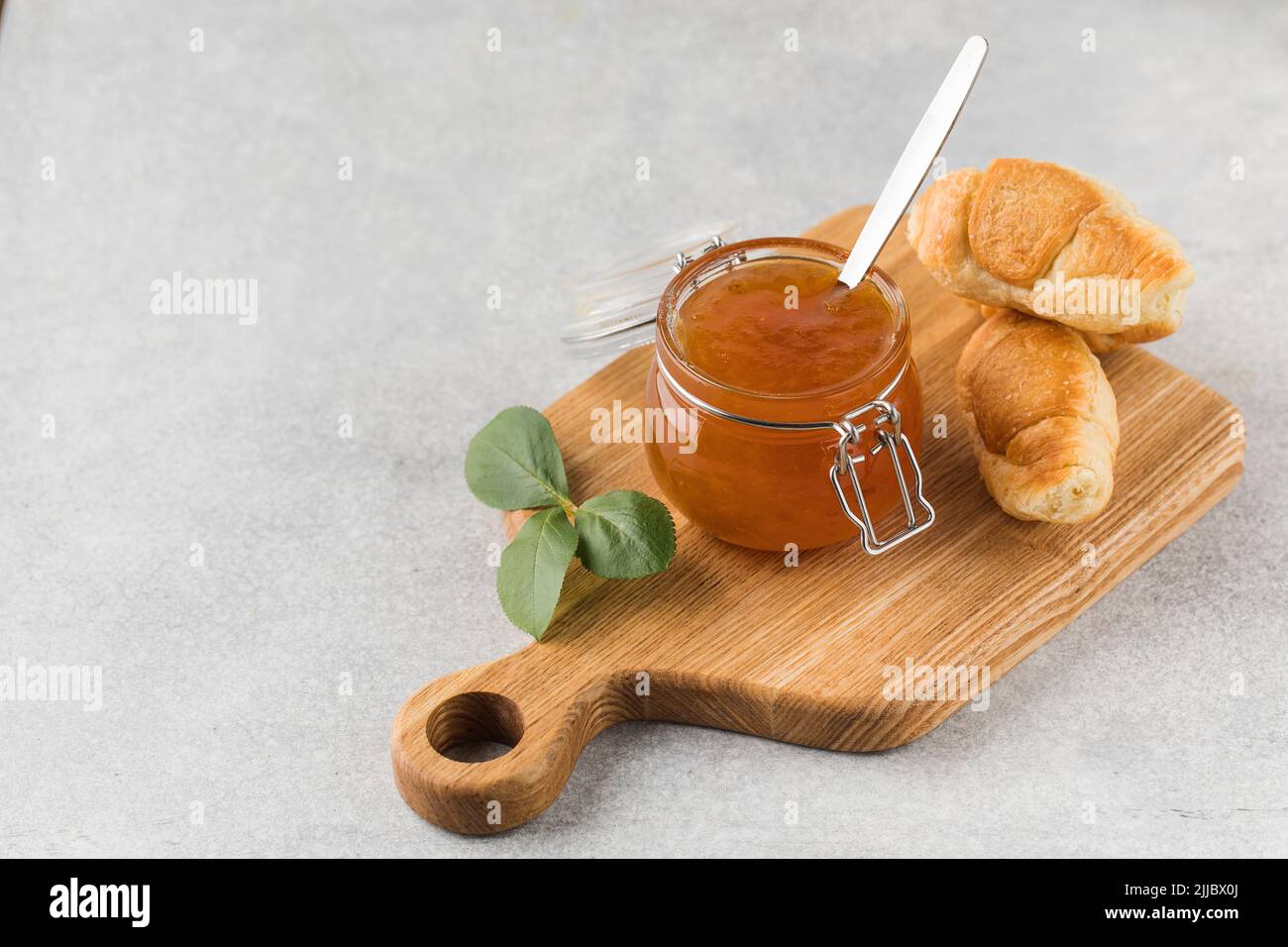 Glass jar with fruity orange jam with croissants on a grey background ...