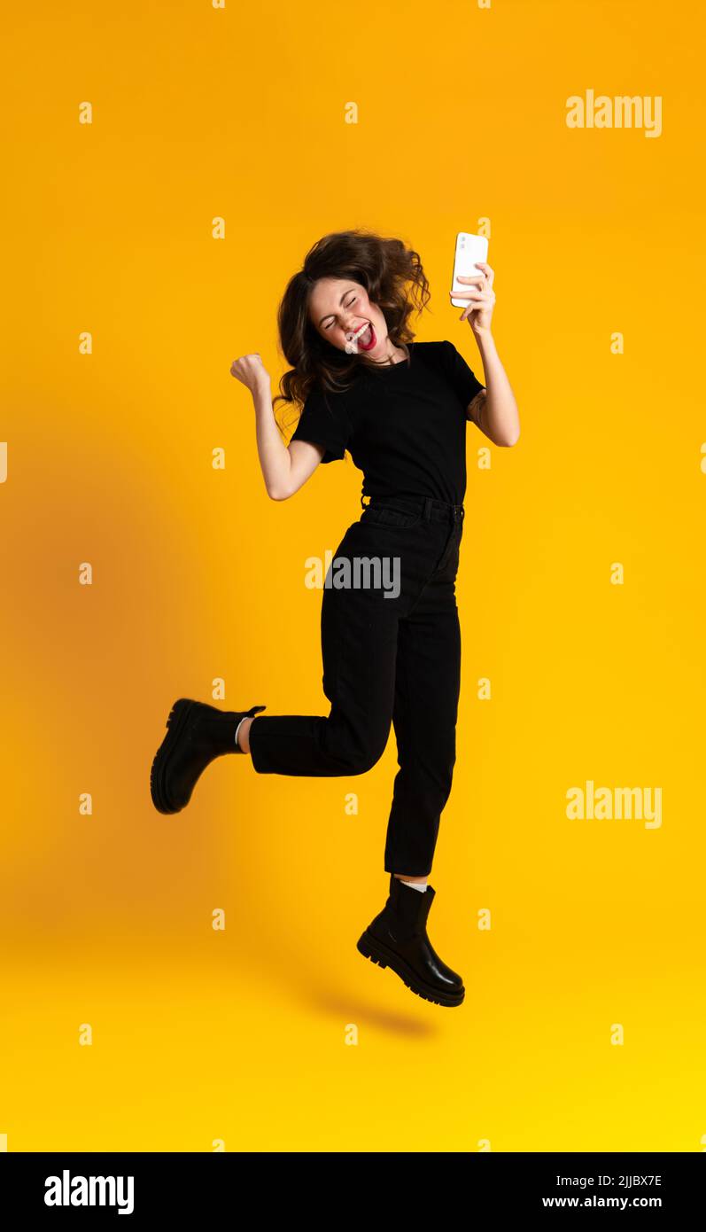 White young woman using mobile phone while gesturing and jumping ...