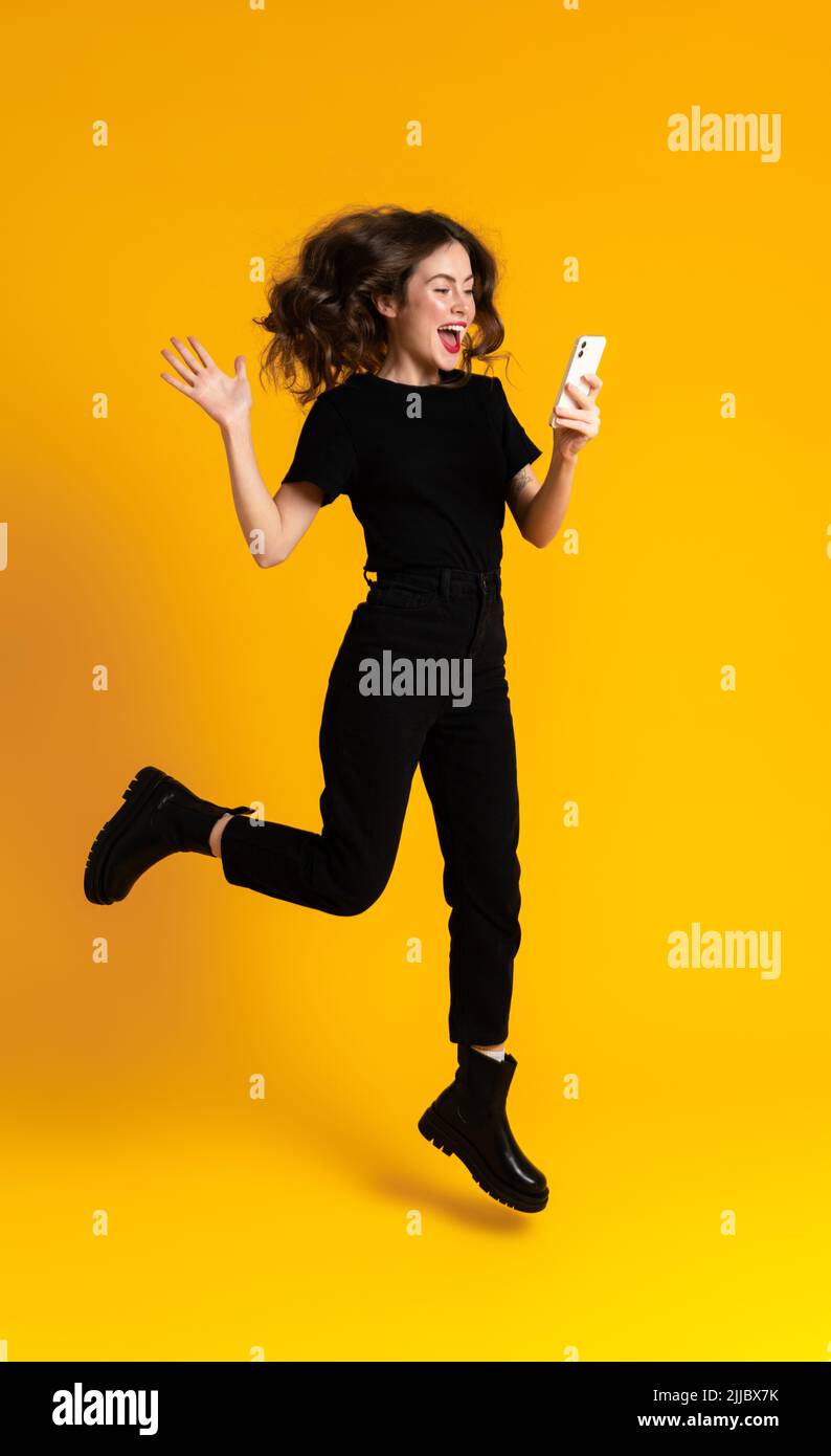 White young woman using mobile phone while gesturing and jumping ...