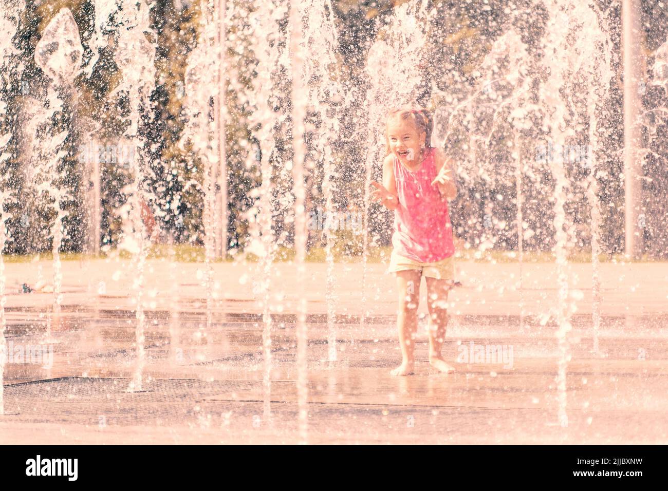 excited baby girl having fun between water jets, in fountain. Summer in ...