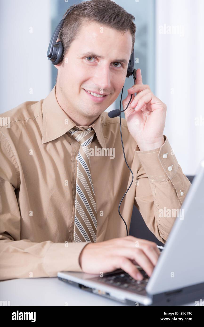 friendly man with a headset is working in home office at a computer ...