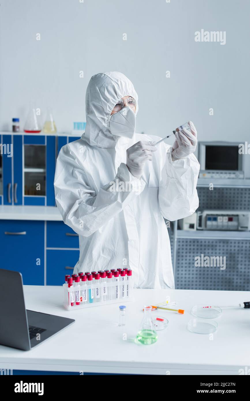Scientist in hazmat suit holding syringe and vaccine near test tubes in ...